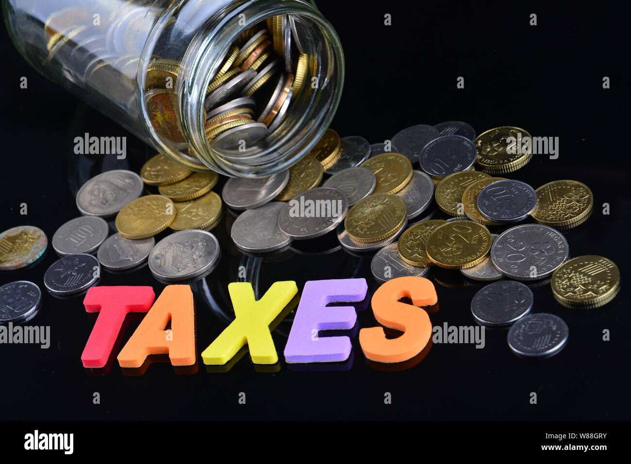 Coins spilling from a money jar with word TAXES Stock Photo - Alamy