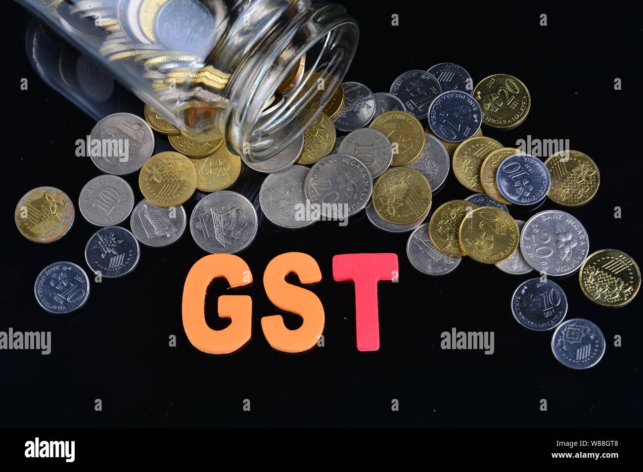 coins spilling from a money jar with word GST Stock Photo - Alamy