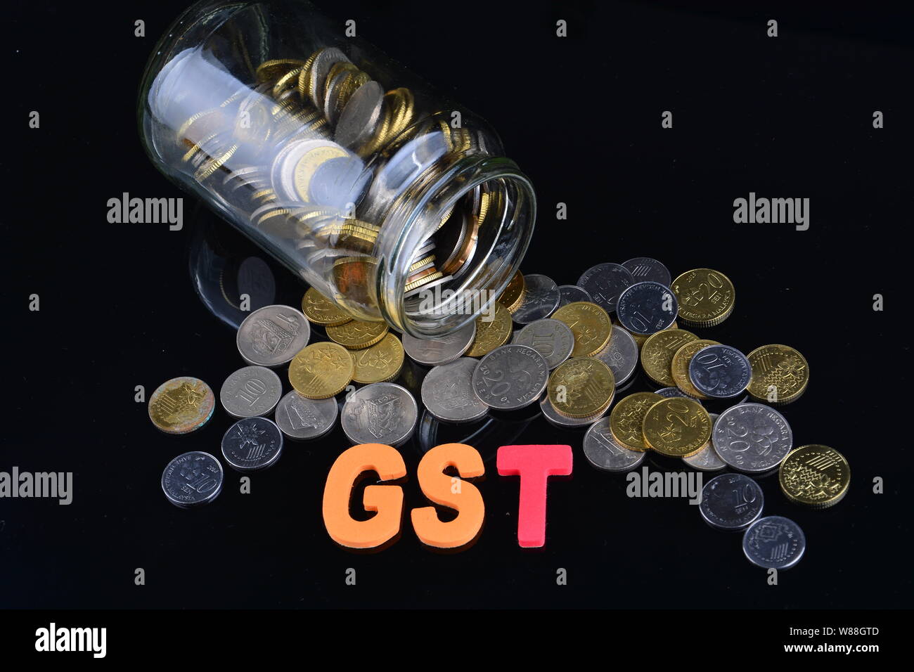 coins spilling from a money jar with word GST Stock Photo - Alamy