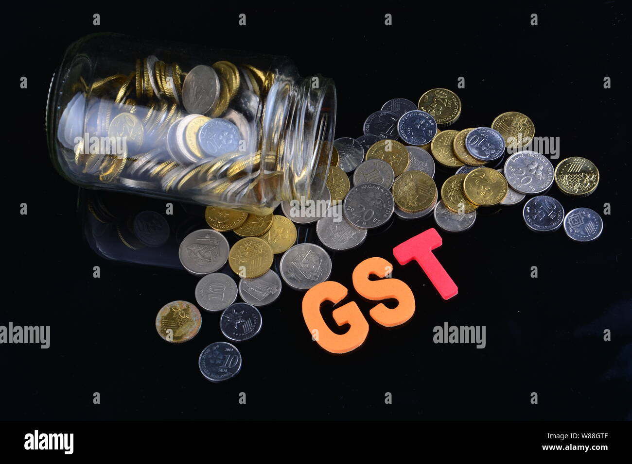 coins spilling from a money jar with word GST Stock Photo - Alamy