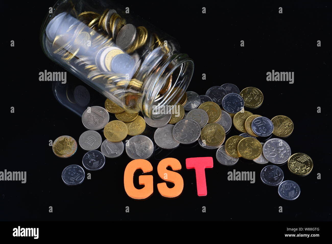 coins spilling from a money jar with word GST Stock Photo - Alamy