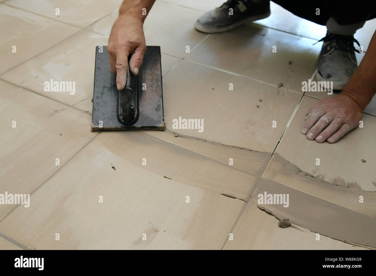 Worker putting fugue on tiles on the floor in corridor. Grouting ...