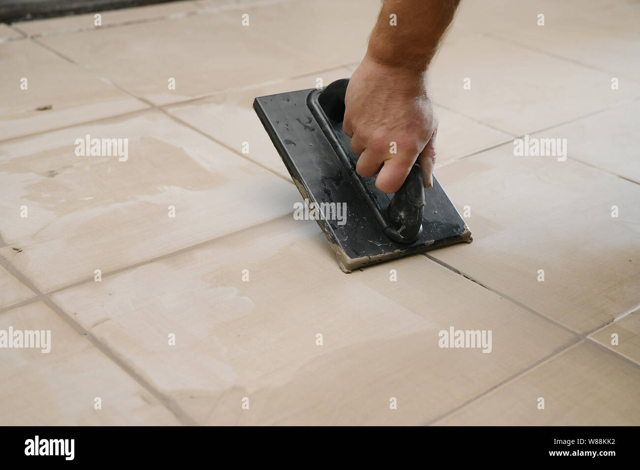 Worker putting fugue on tiles on the floor in corridor. Grouting ...