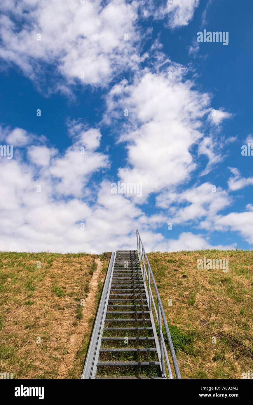 Metal staircase to the top of a dike, yellow grass and blue sky with ...