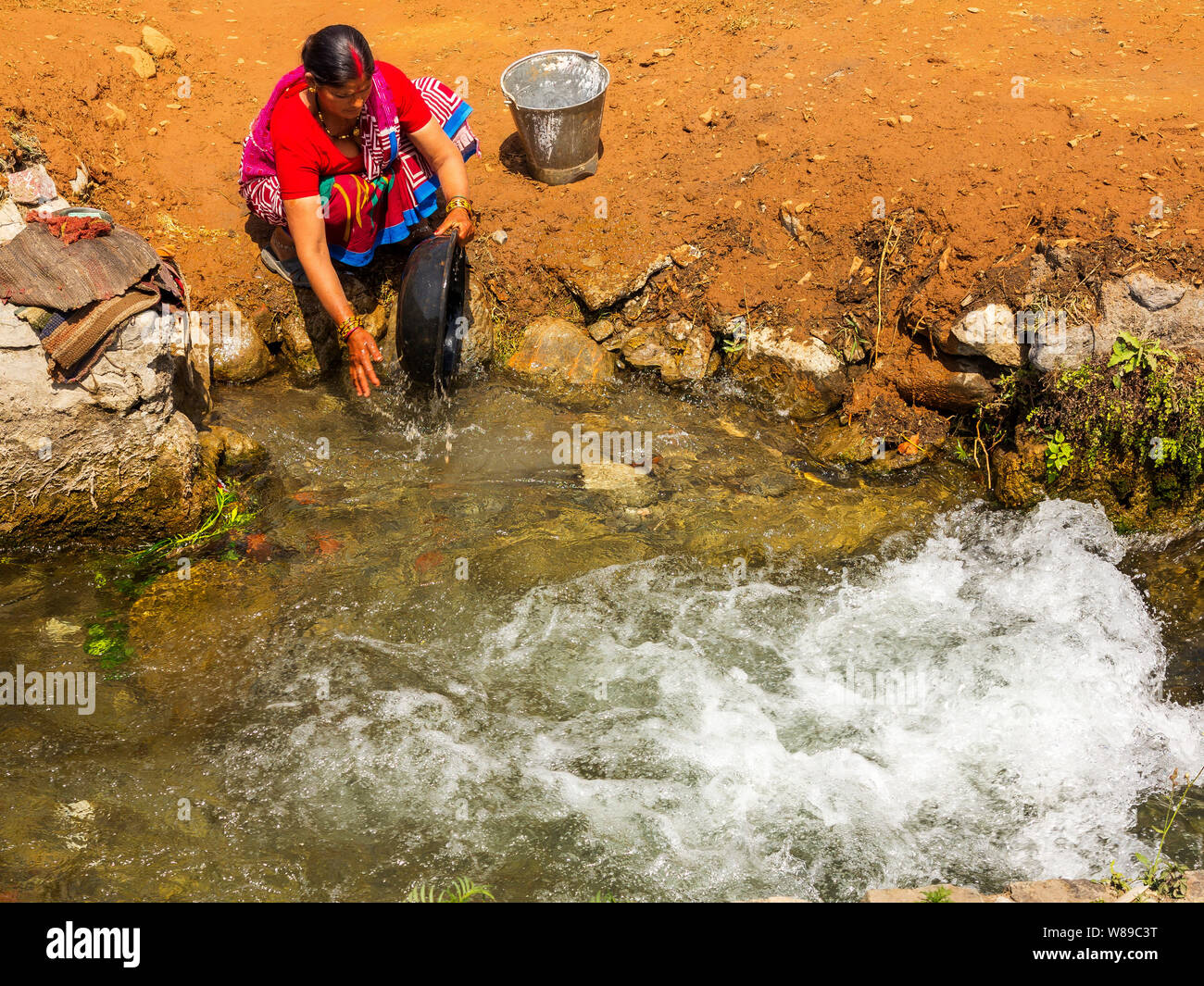 Indian woman washing utensils at the canal at Pawalgarh village ...