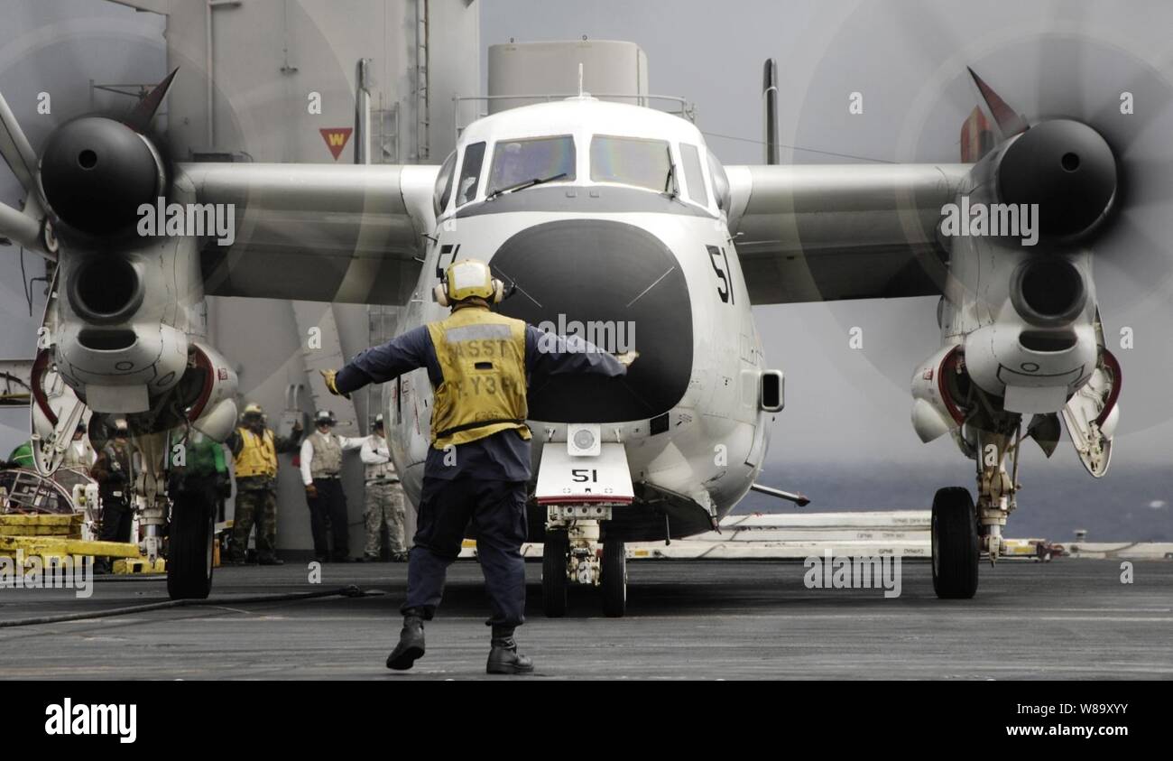 An aircraft director guides a C-2A Greyhound aircraft across the flight ...