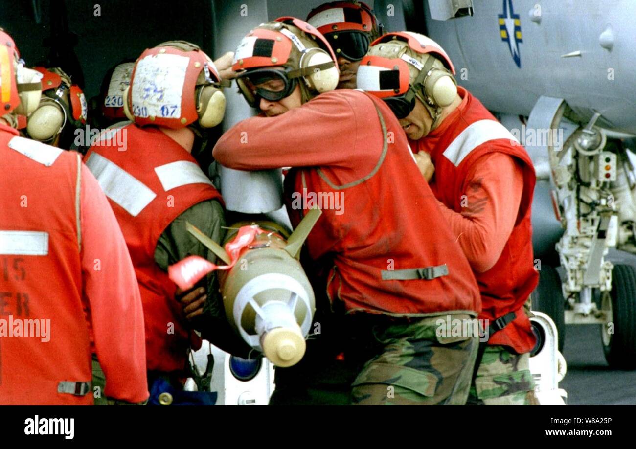 Red-shirted aviation ordnancemen use muscle to lift a laser guided bomb ...