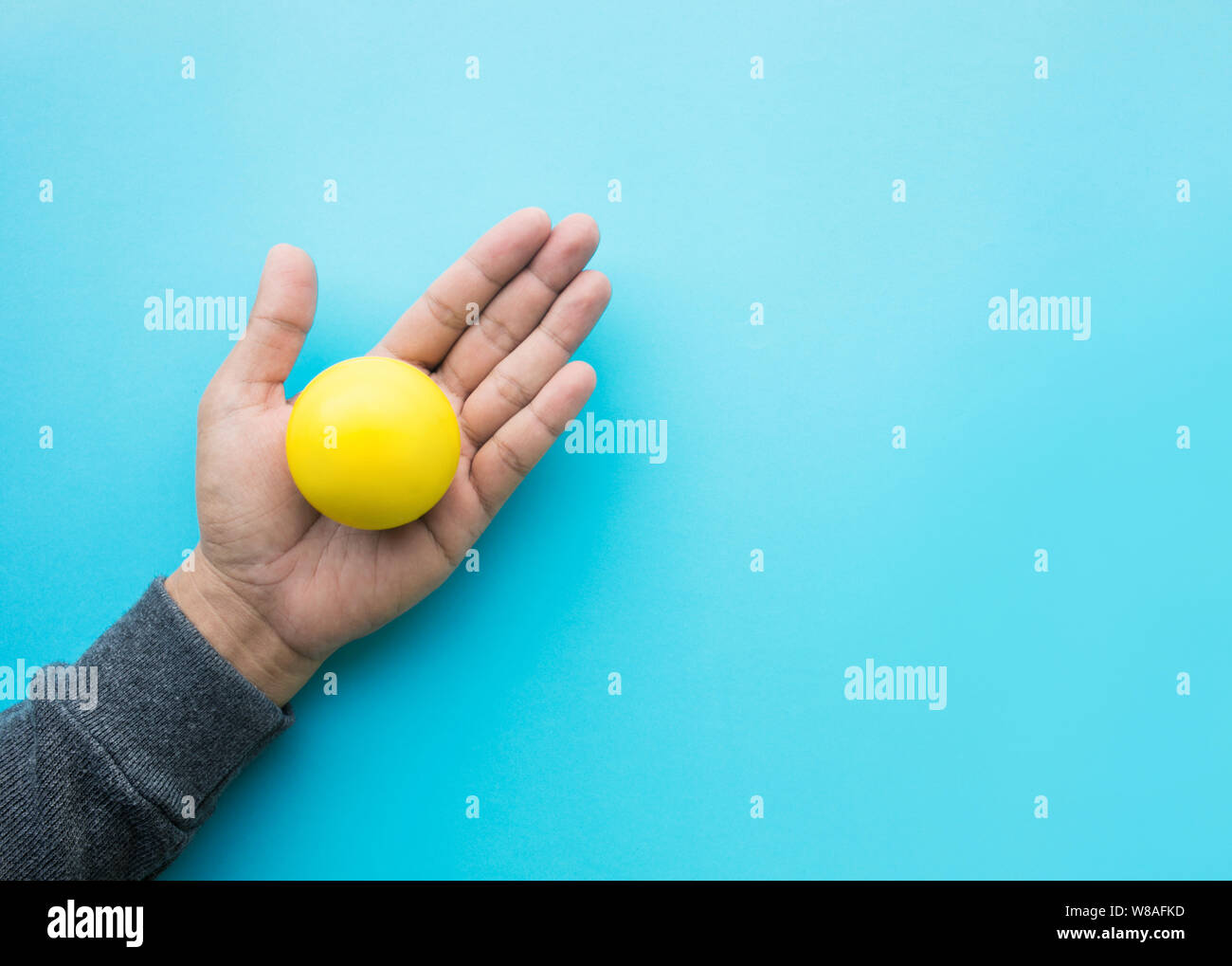 Mele hand holding yellow ball on blue color background Stock Photo - Alamy