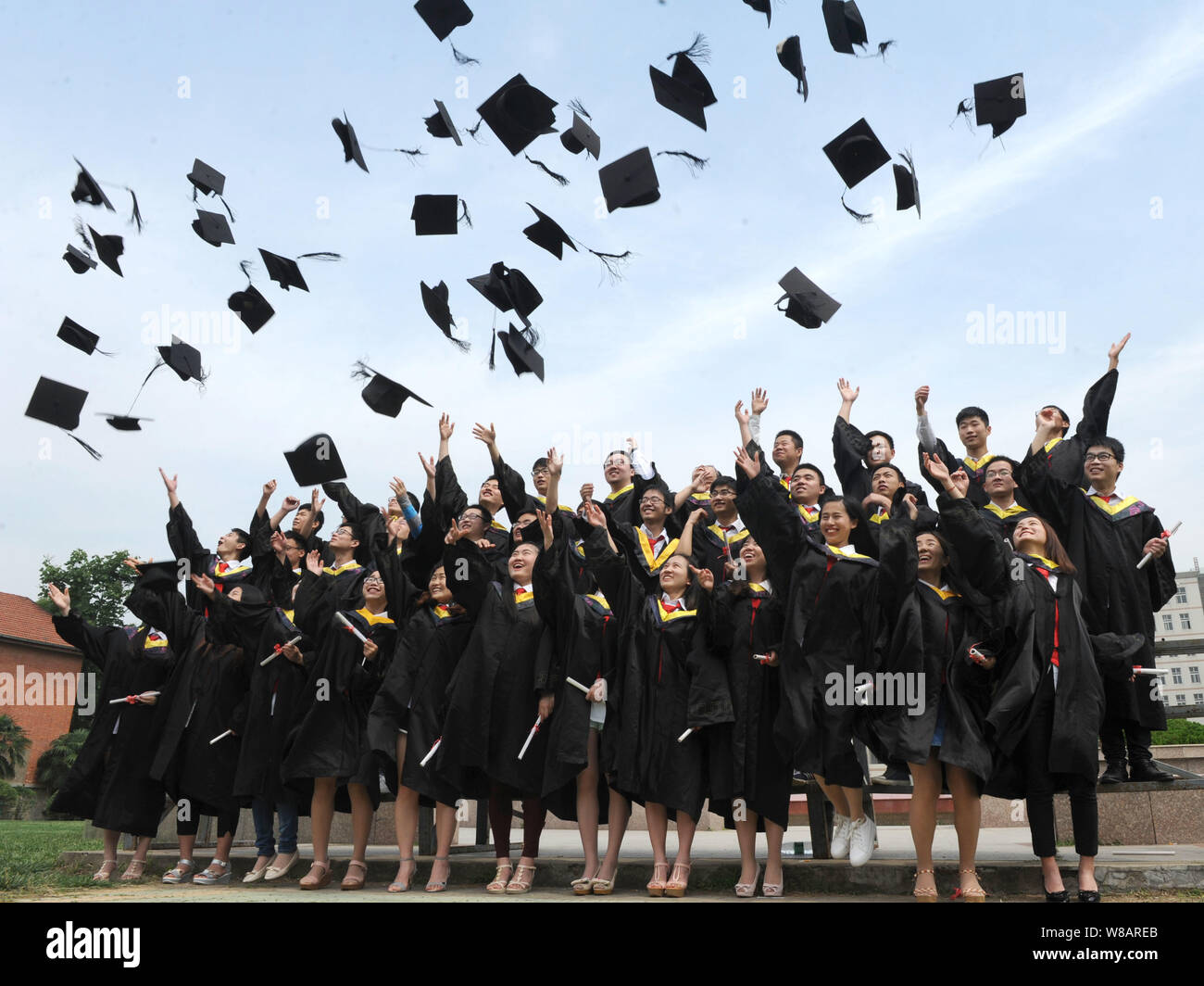 --FILE--Chinese graduates dressed in academic gowns throw their hats ...