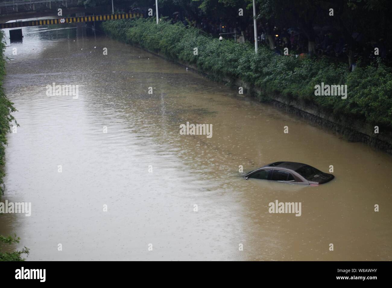 A car is half-submerged on a flooded road caused by heavy rain in ...