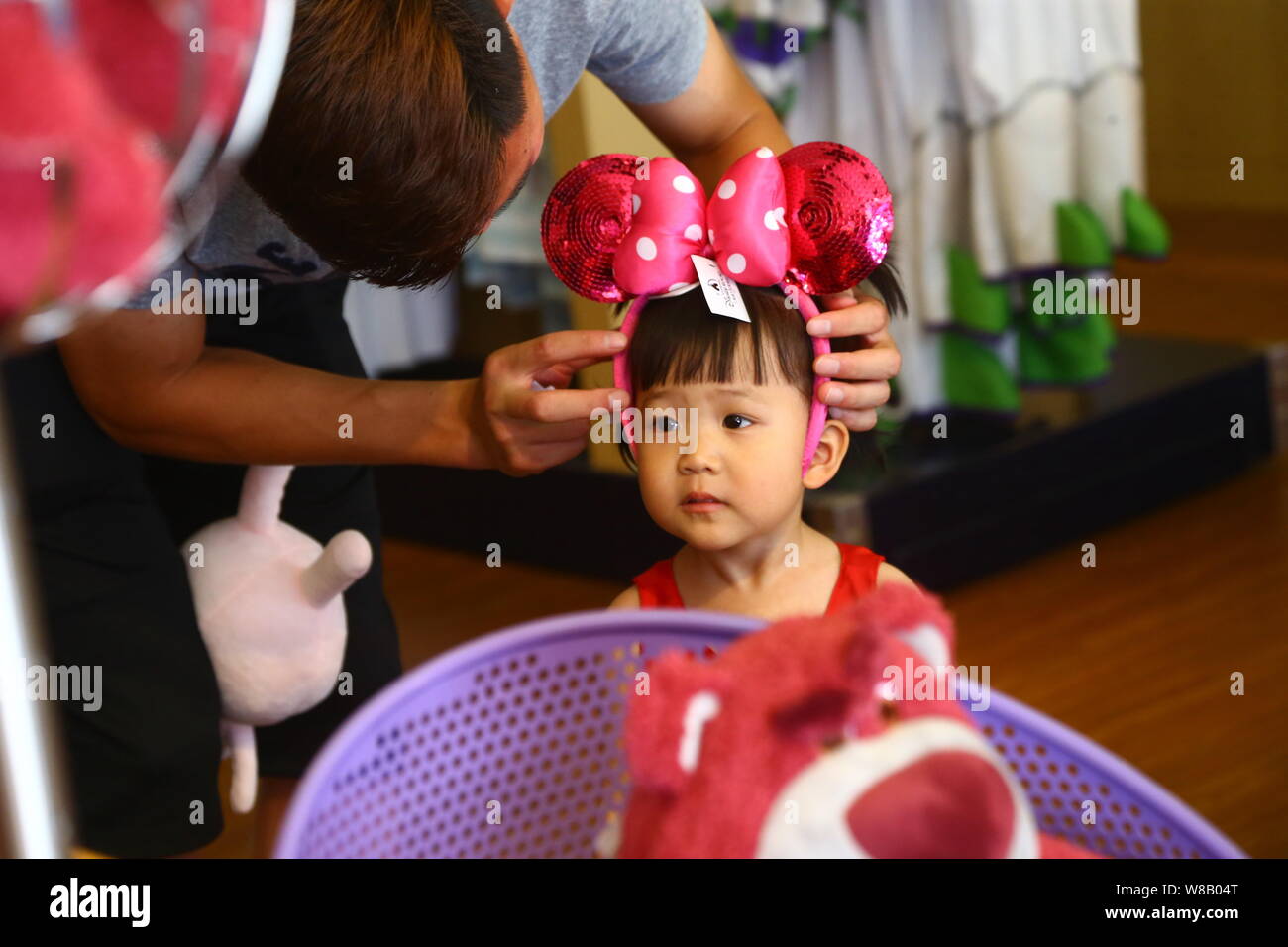 A father helps his daughter put on a Minnie Mouse headwear in a shop in ...