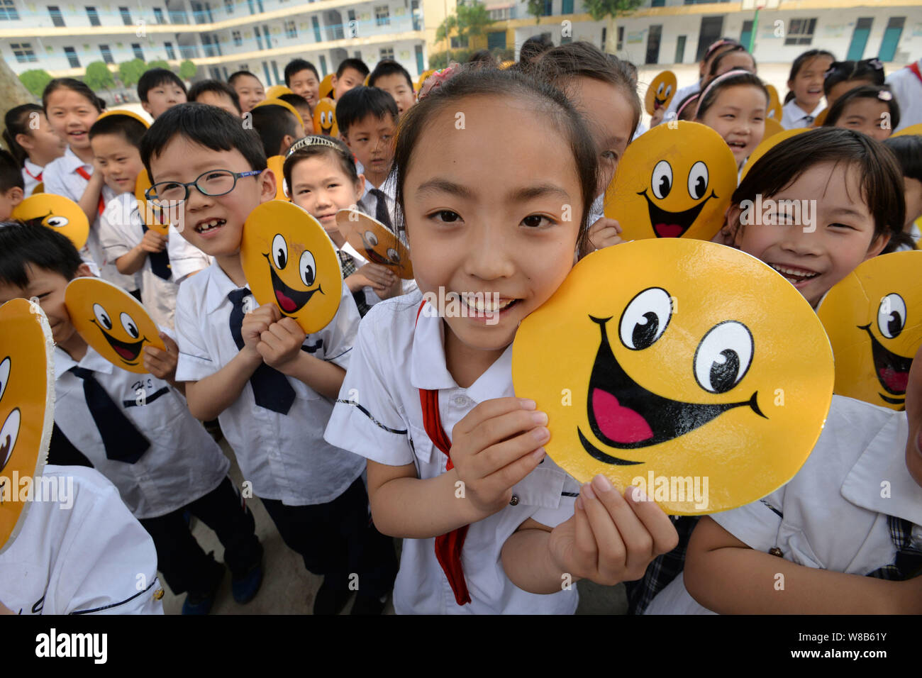 Young Chinese students smile and hold up smiling-face cutouts to ...