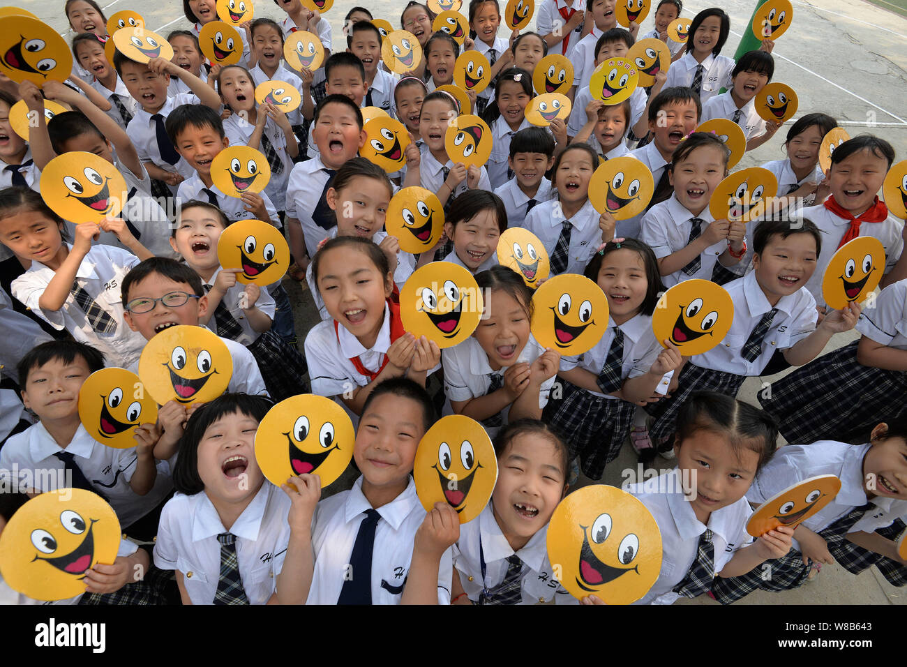 Young Chinese students smile and hold up smiling-face cutouts to ...