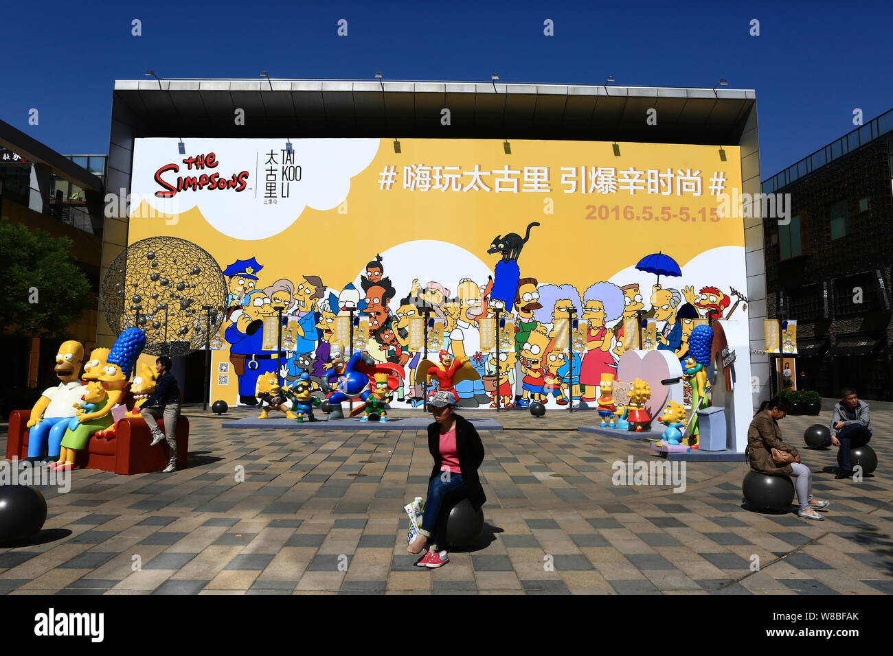 People rest next to model figures of The Simpsons on display in front ...