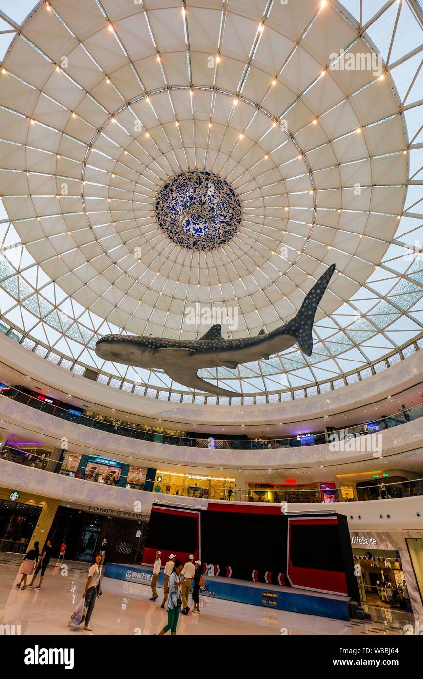 People walk under a model shark in the Wanda Mall at the Nanchang Wanda ...
