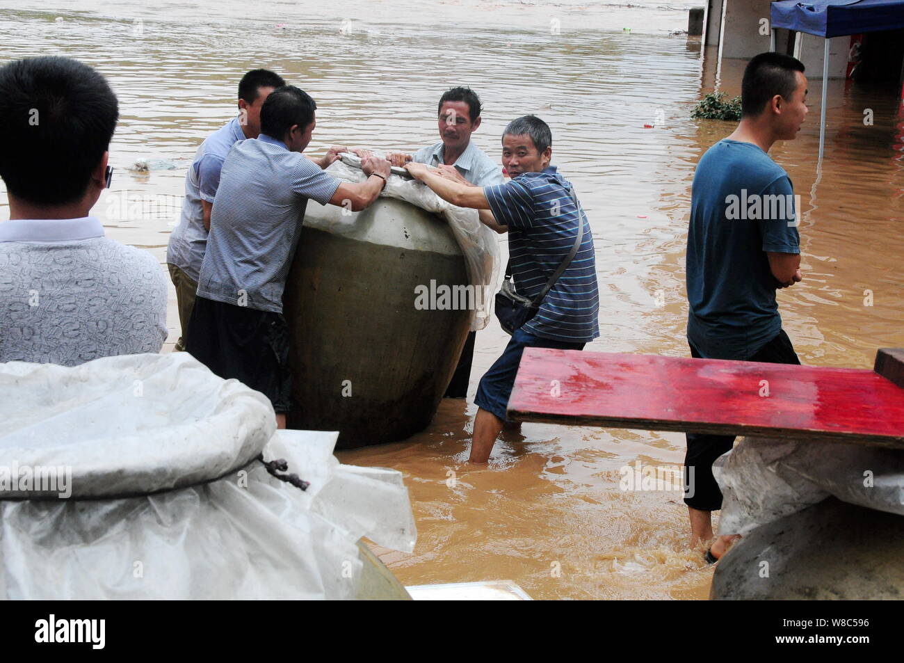 Local Chinese residents try to move a big jar out of the flooded area ...