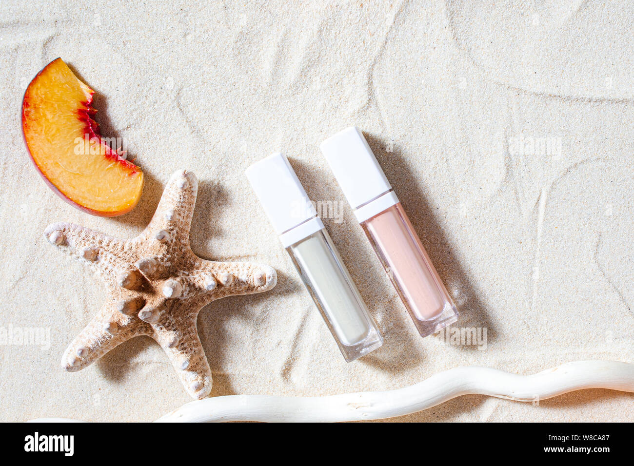 Vacation. Lip gloss in a transparent tube lies on the sand, surrounded ...