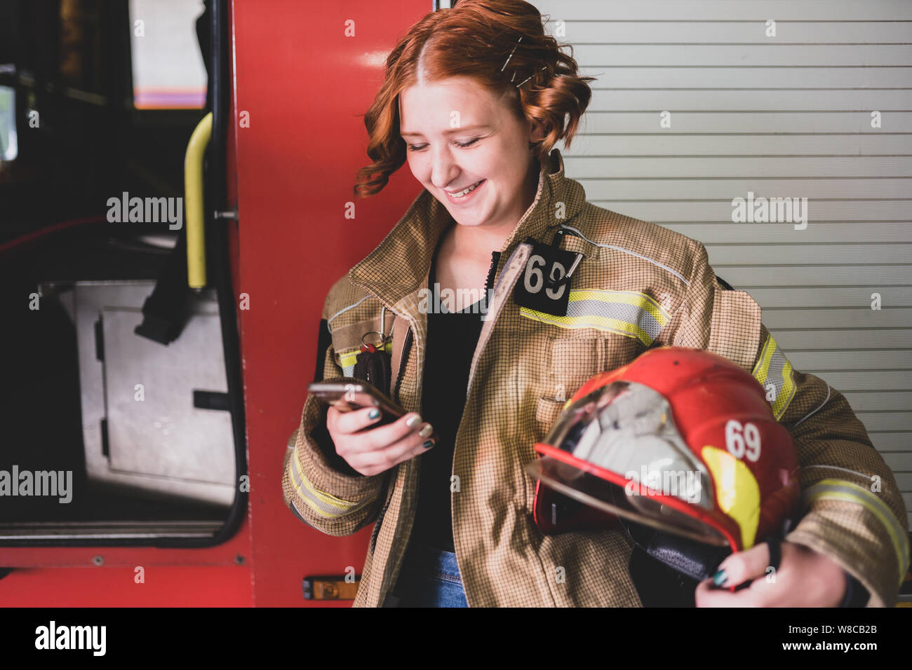 Photo of ginger woman firefighter with phone in her hands against ...