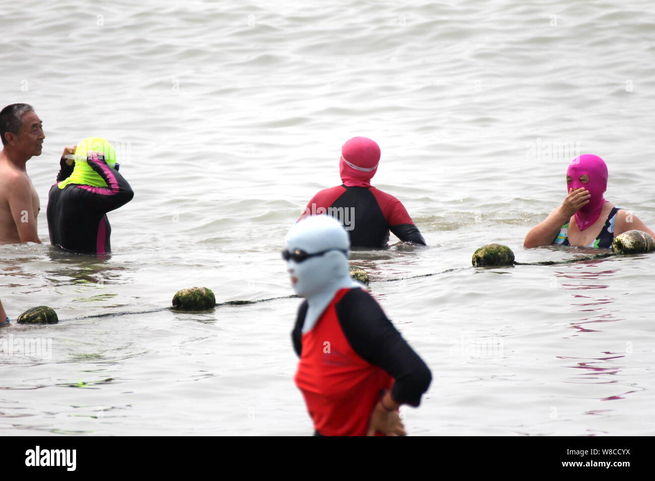 Female Chinese swimmers wearing facekinis swim in the water at a beach ...