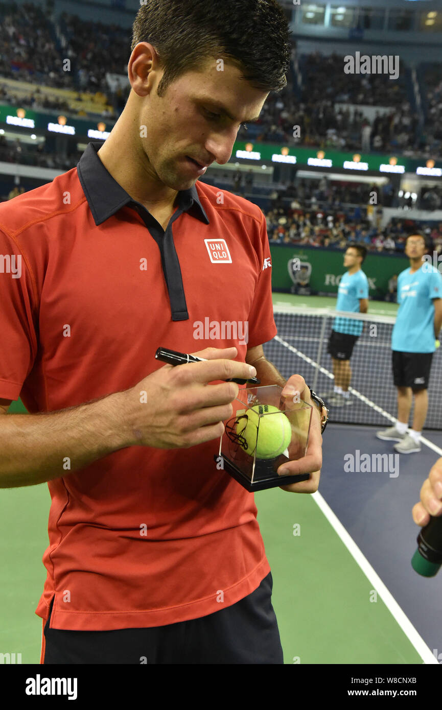 Novak Djokovic of Serbia, left, signs an autograph on a tennis ball ...