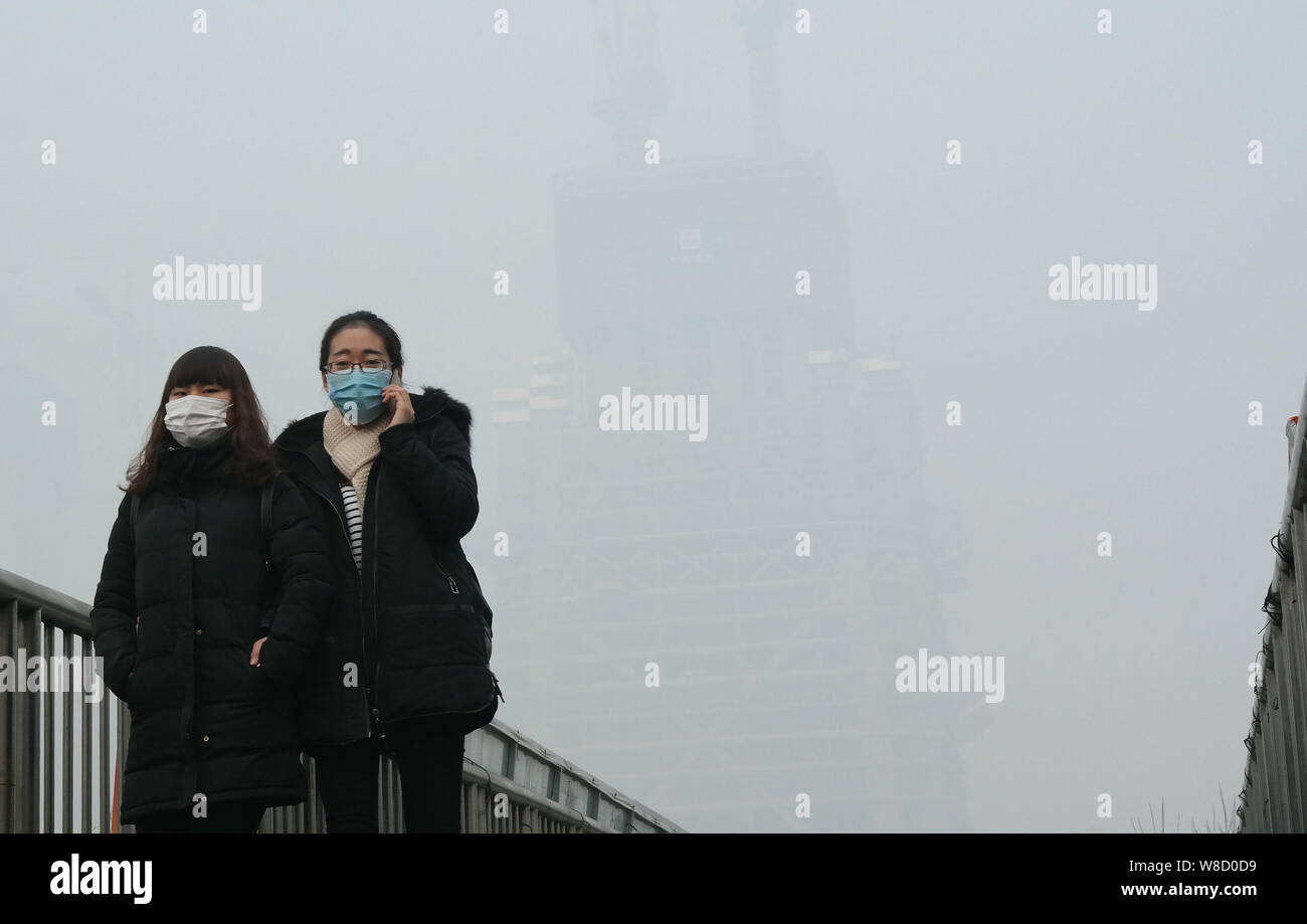 Pedestrians wearing face masks walk across a footbridge in heavy smog ...