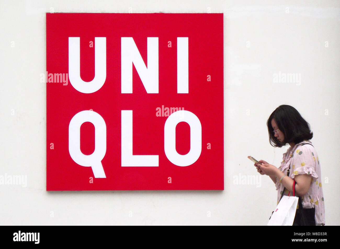 --FILE--A pedestrian using her smartphone walks past a signboard of ...