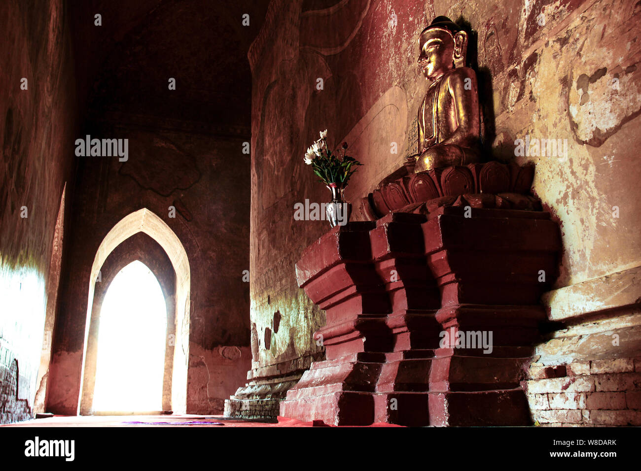 Old golden buddha statue on an altar with white flowers in a buddhist ...