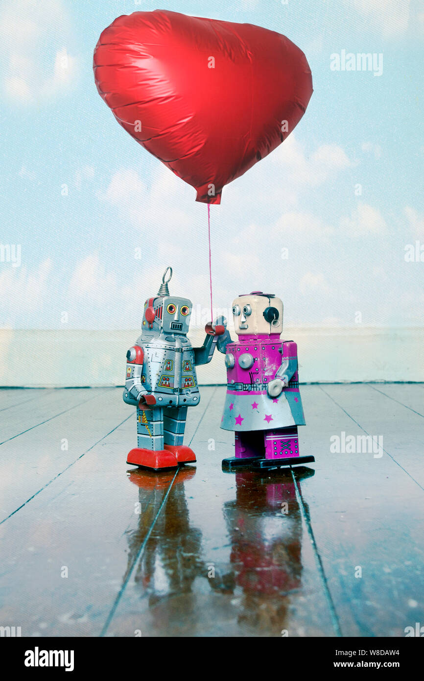 two robots in love holding a red balloon standing on a old wooden floor ...