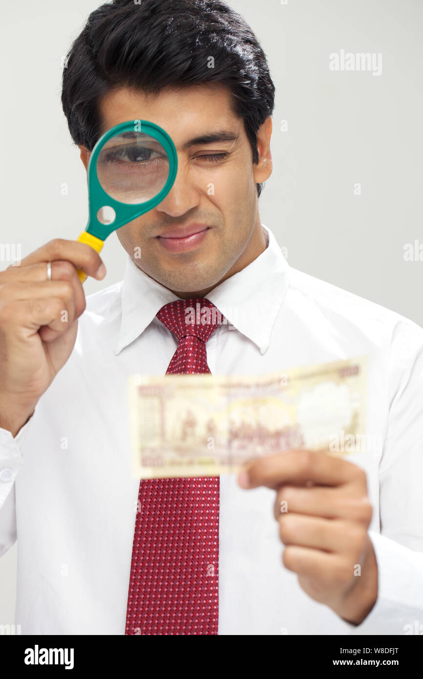Businessman examining five hundred rupee note banknote with magnifying ...