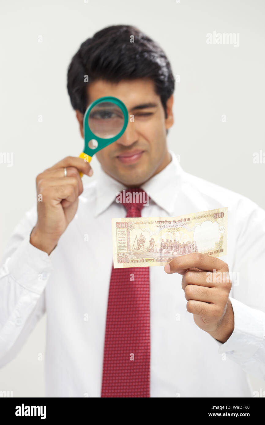 Businessman examining five hundred rupee note banknote with magnifying ...