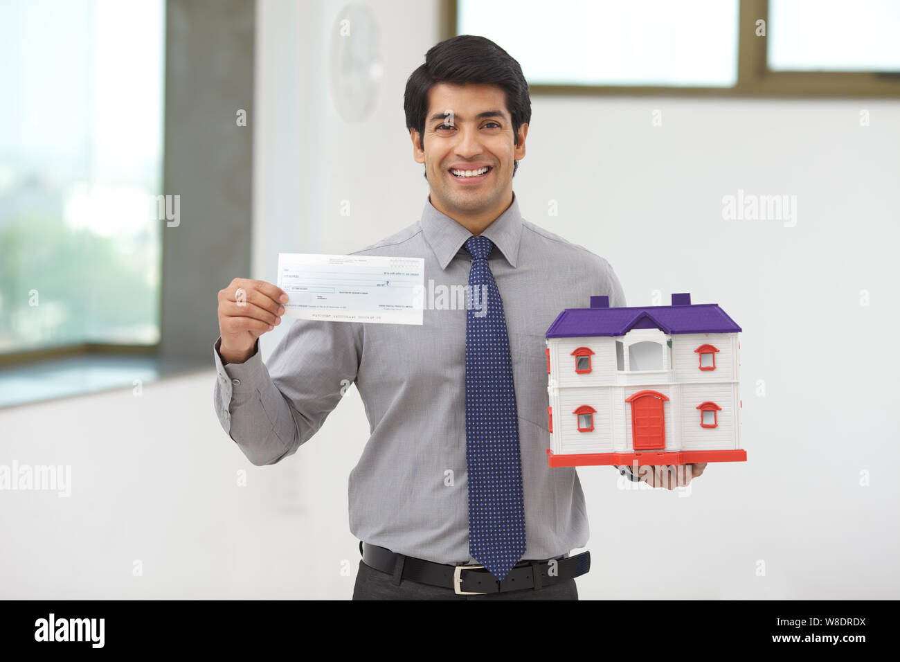 Real estate agent holding a miniature house and showing a cheque Stock ...