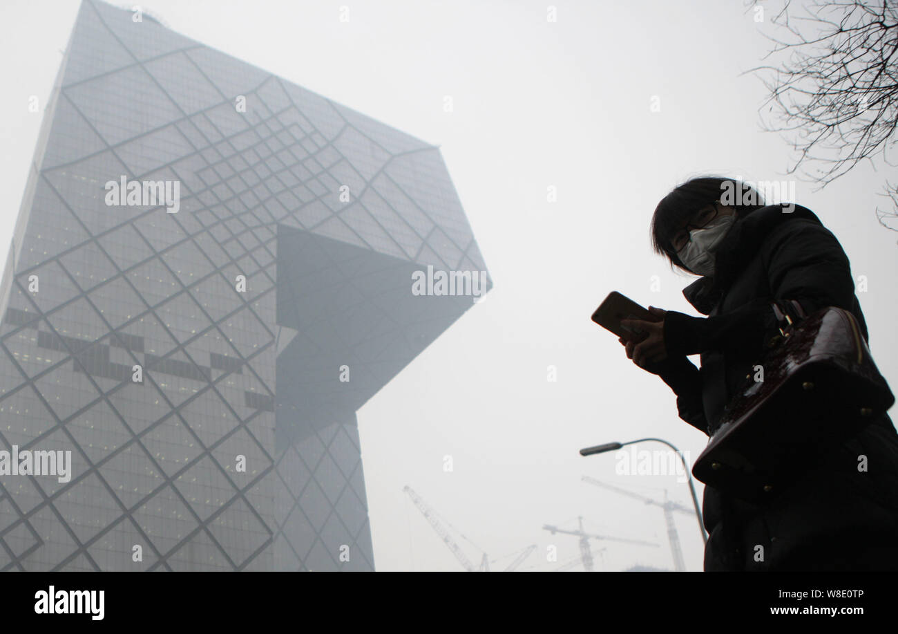 A pedestrian wearing a face mask uses her mobile phone as she walks ...