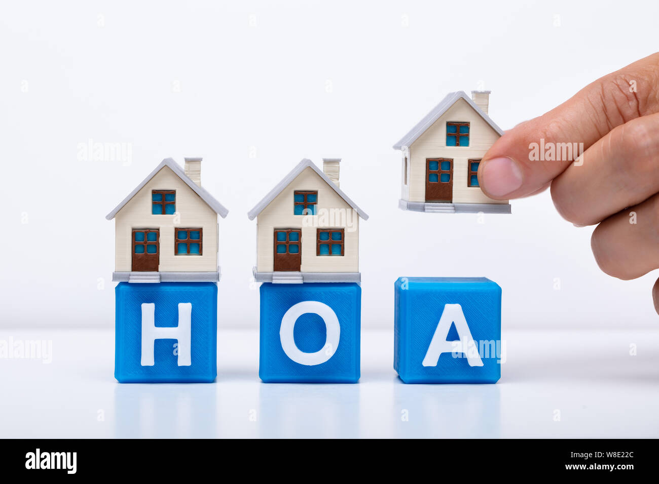 Businessperson's Hand Placing House Model Over Red HOA Blocks On Wooden ...