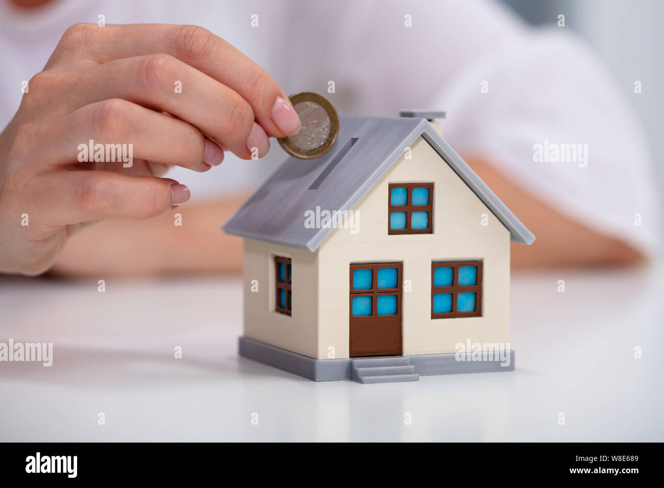 Close-up Of A Woman Inserting Coin In House Piggybank Stock Photo - Alamy