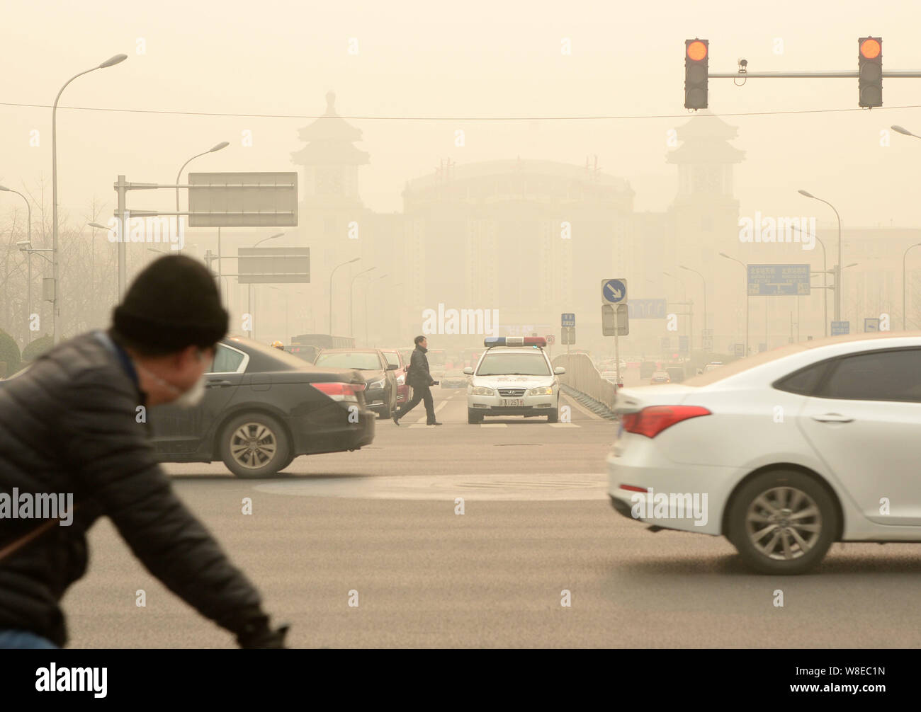 Cyclists and cars pass by the Beijing Railway Station vaguely seen in ...