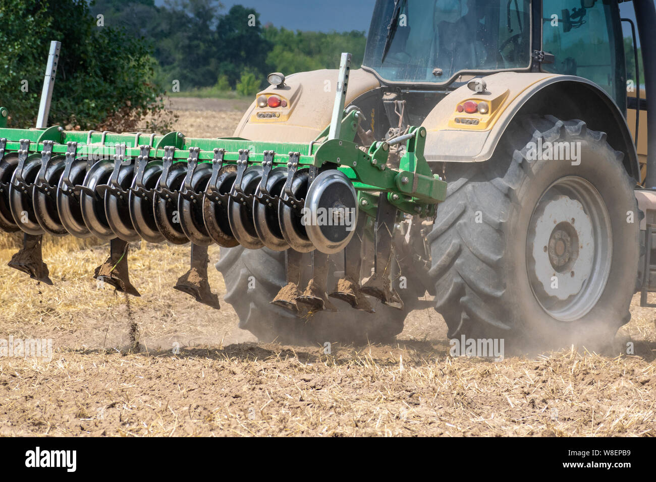 Yellow tractor cultivating the field after harvesting rear view closeup ...