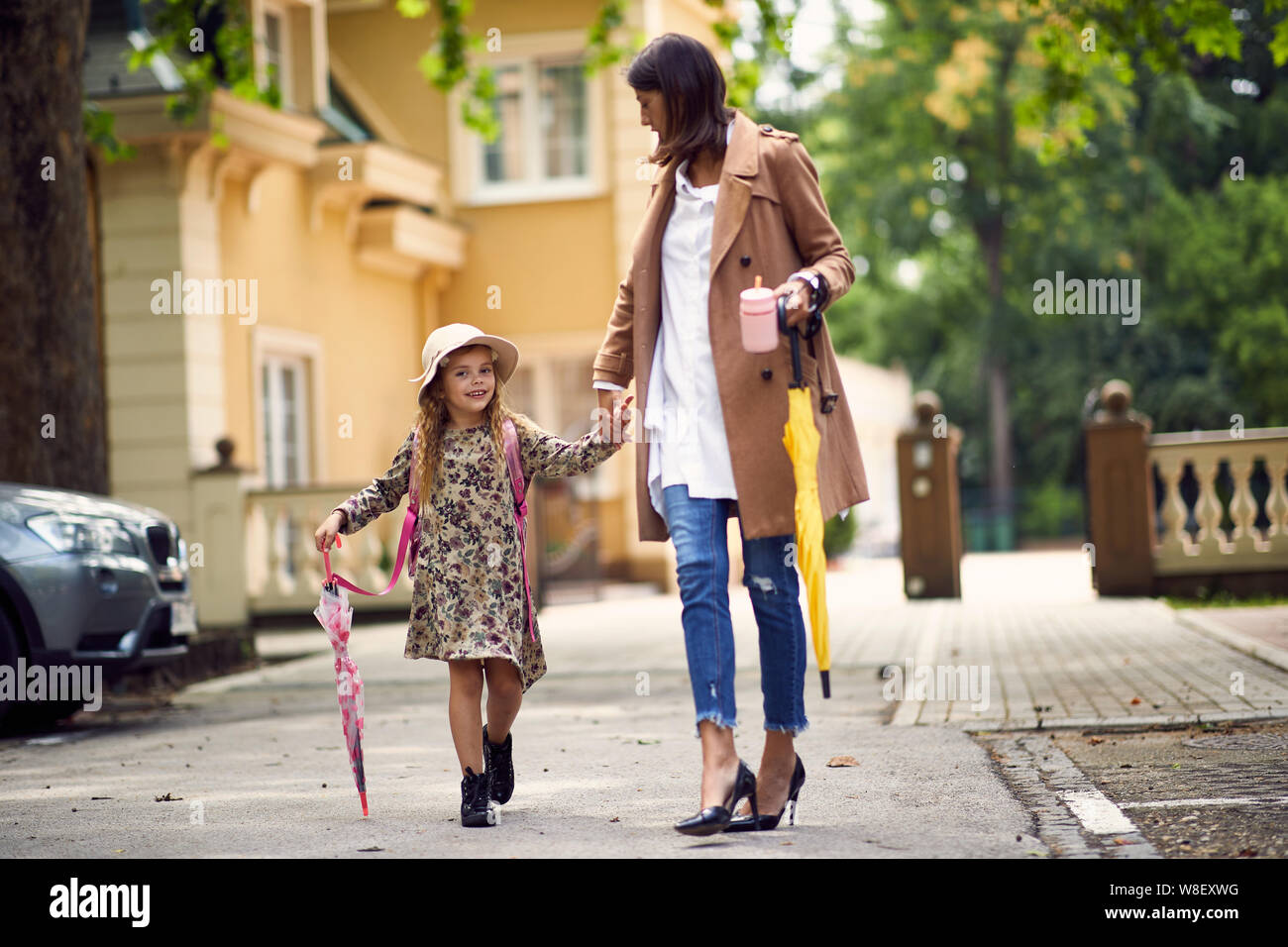 Happy mother and daugther go to elementary school. Parent taking child ...