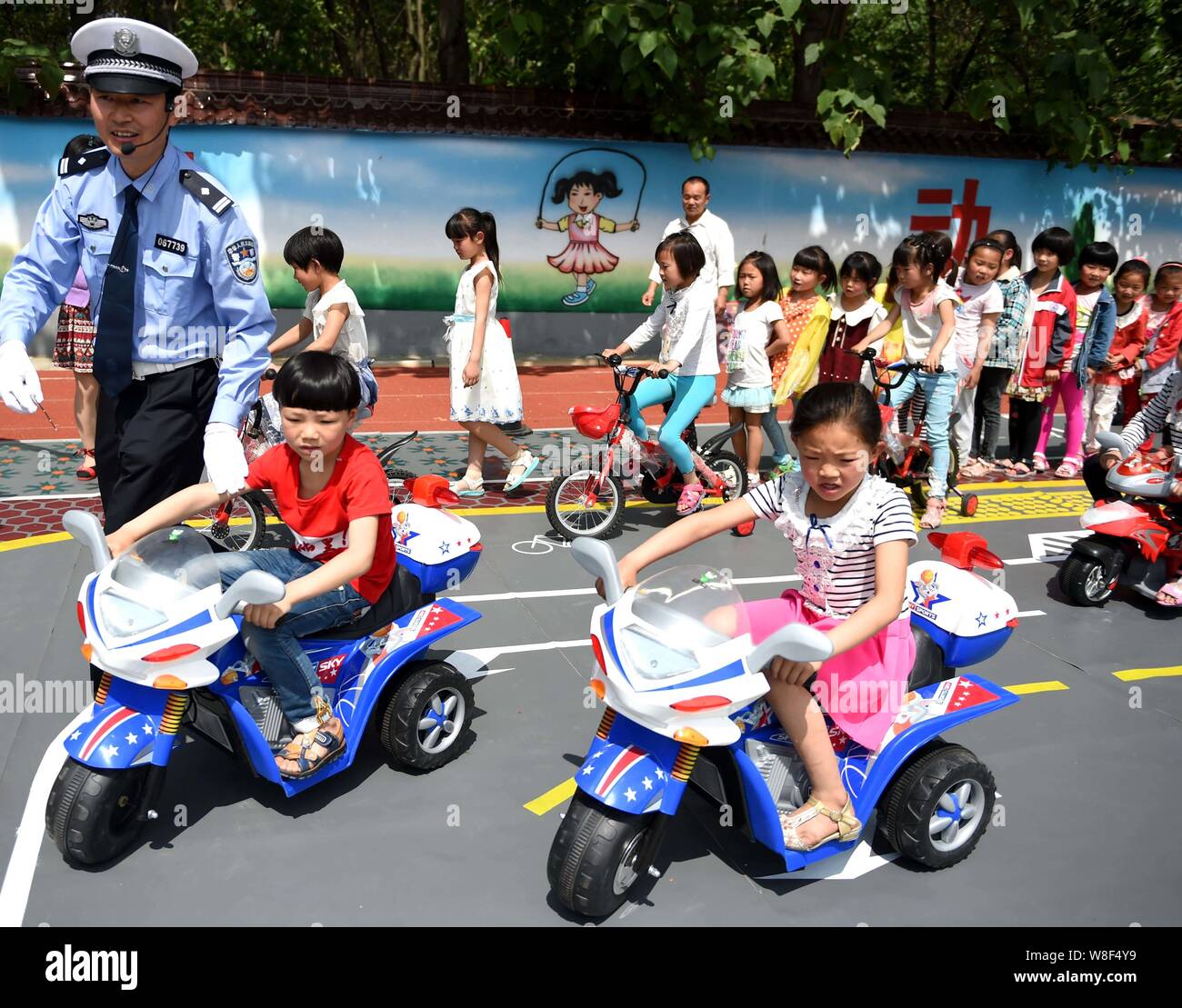 A police officer directs young students to ride toy tricycles on a mock ...