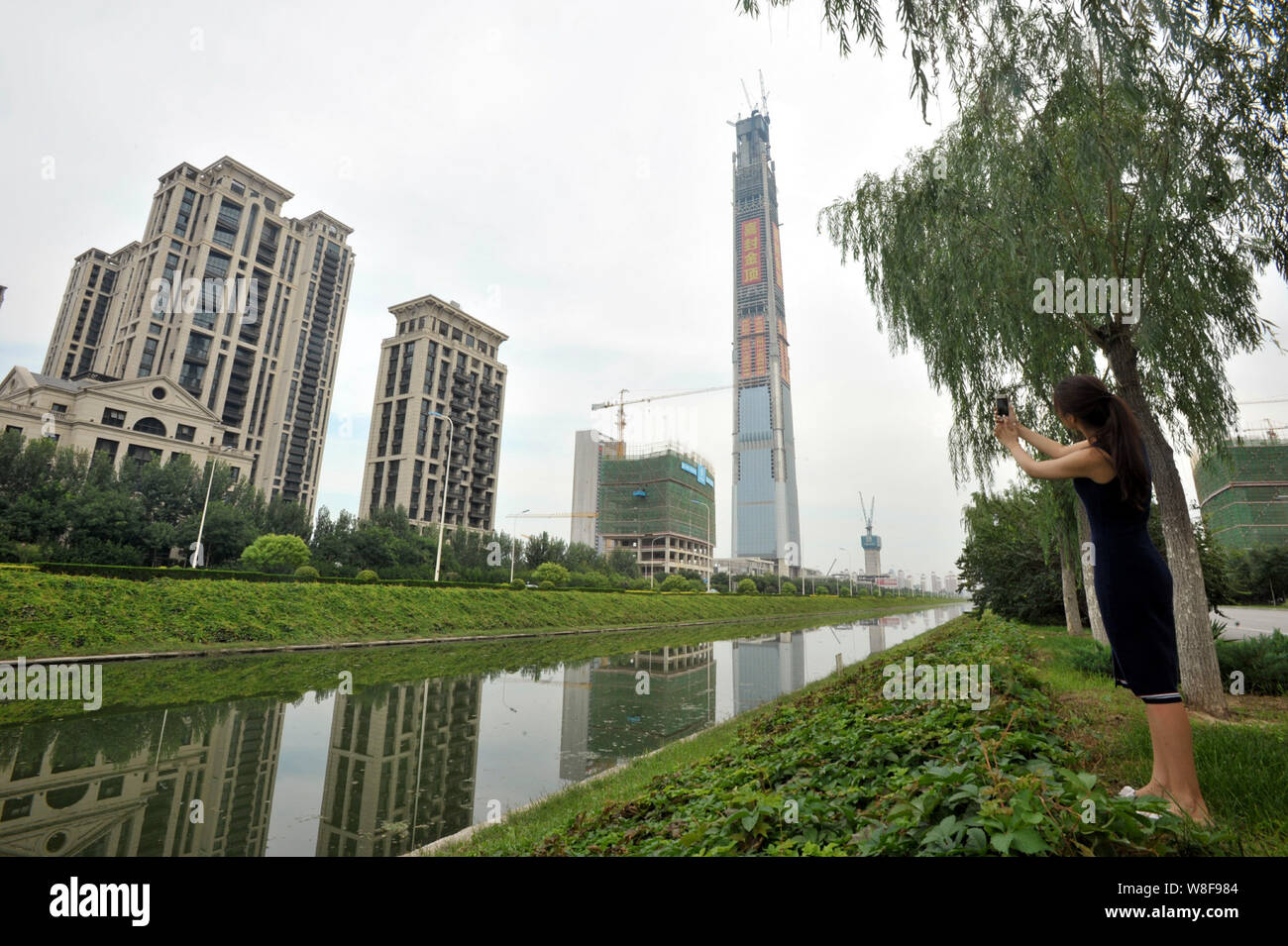 A pedestrian takes pictures of the 117-story Tianjin 117 Tower under ...