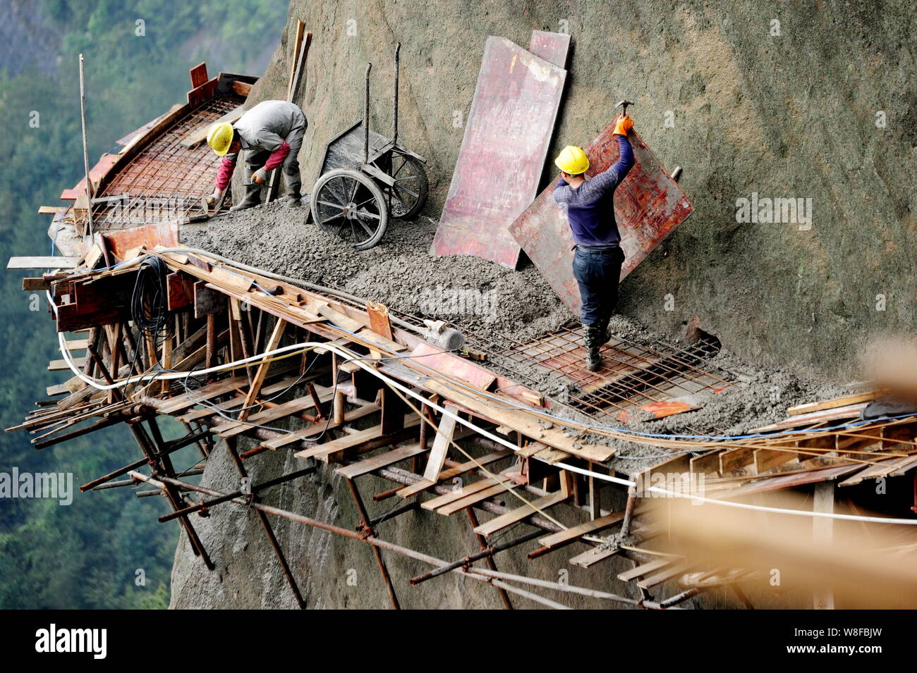 Workers pave a road with cement and planks on the cliff of a mountain ...
