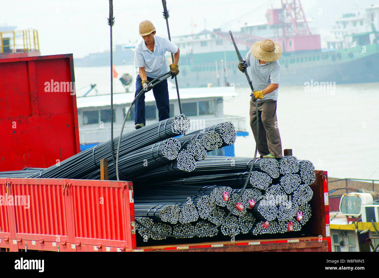 --FILE--Chinese workers unload reinforcing steel rods from a truck at a ...
