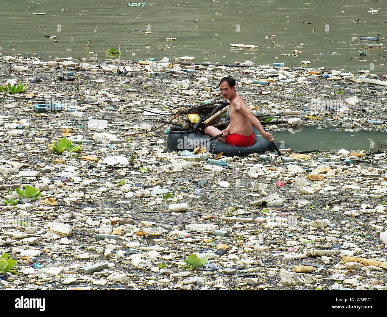--FILE--A Chinese man sitting on a life buoy rows among garbage ...