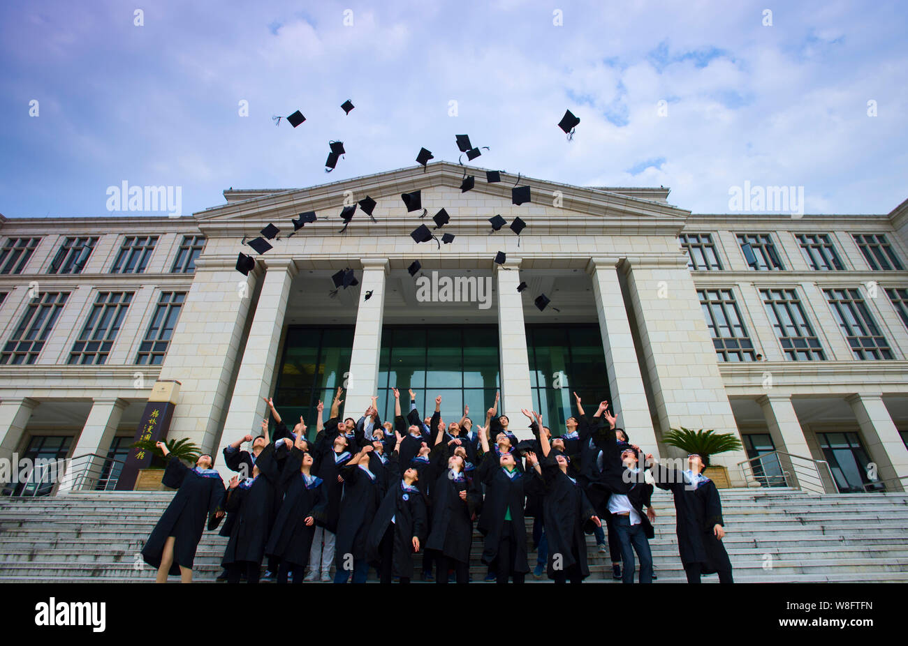 Chinese graduates dressed in academic gowns throw hats into the air to ...