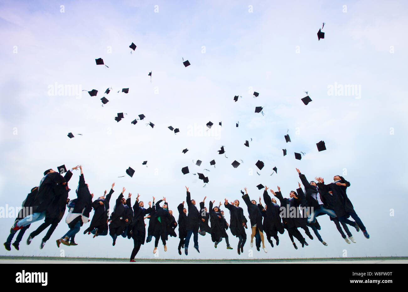 Chinese graduates dressed in academic gowns throw hats into the air to ...