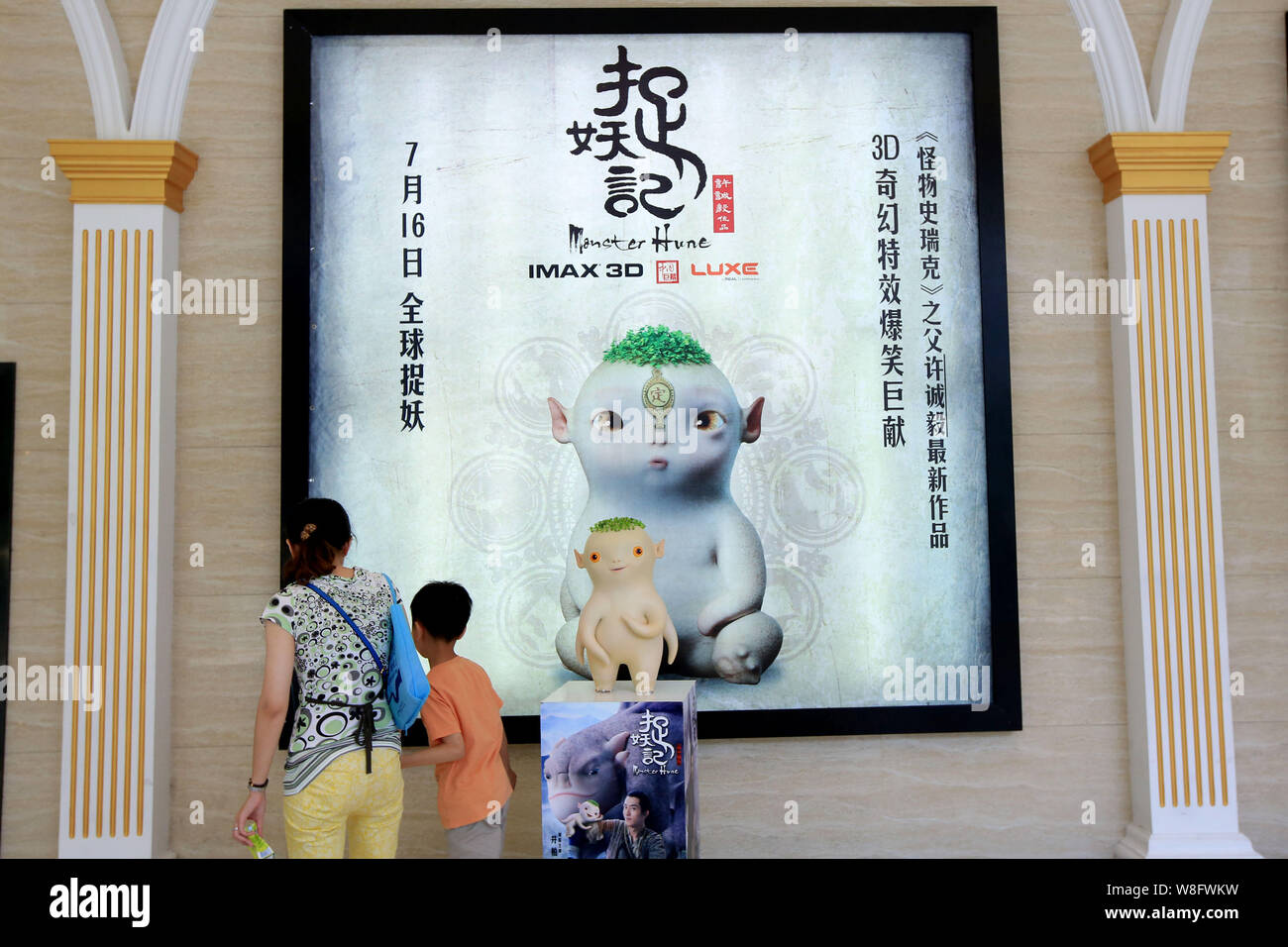 People walk past a poster of the movie "Monster Hunt" and a model of ...