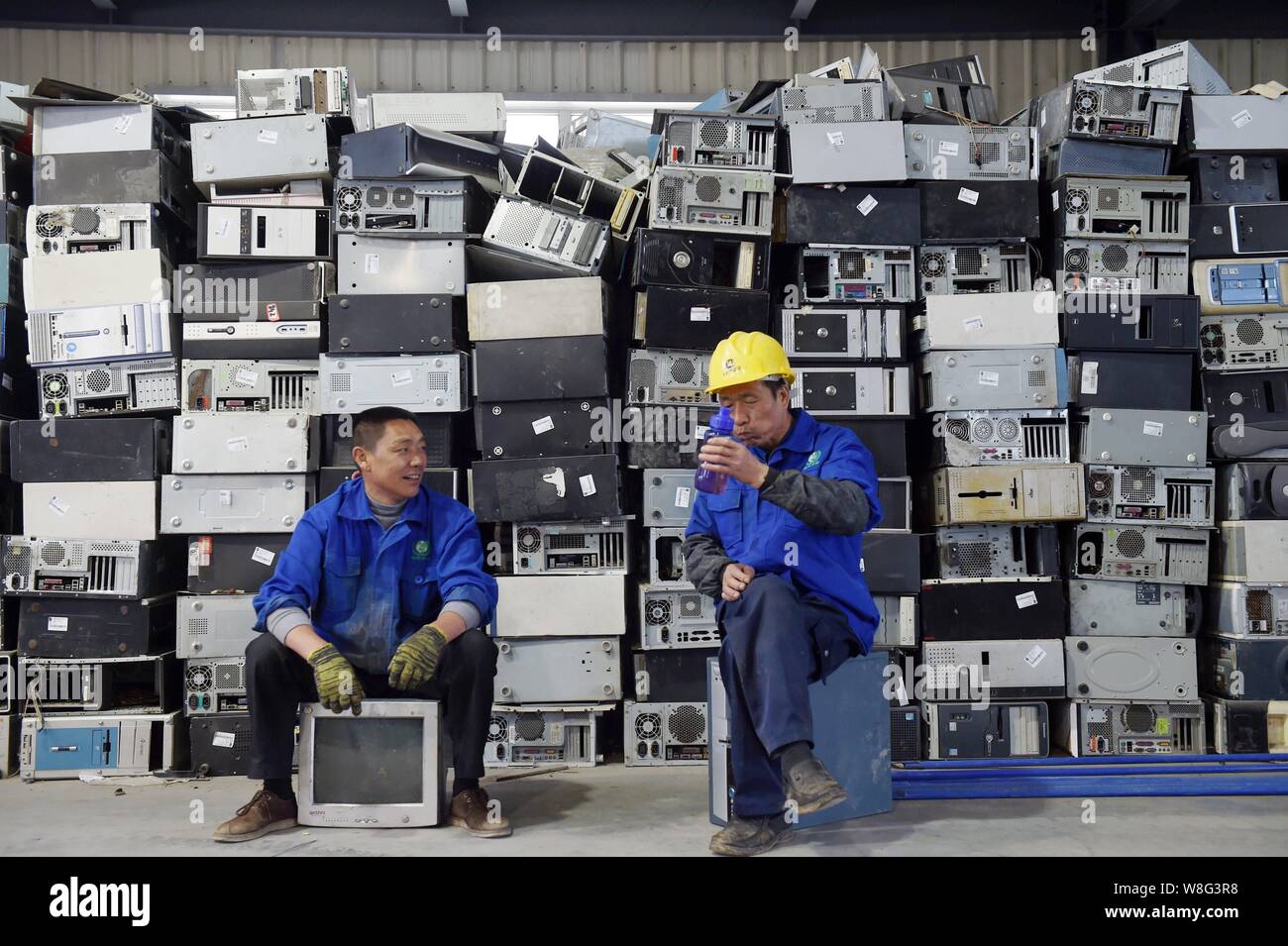 Two Chinese workers talk in front of piles of discarded desktop ...