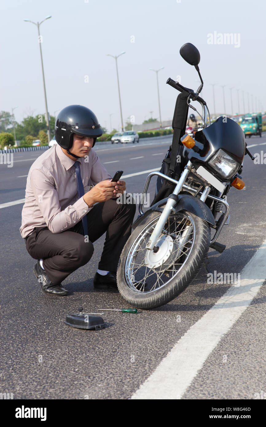 Sales executive examining the tire of his motorcycle and using a mobile ...
