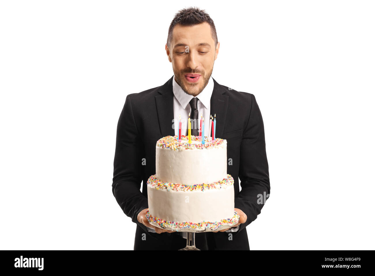 Young man in a suit holding a birthday cake and blowing candles ...