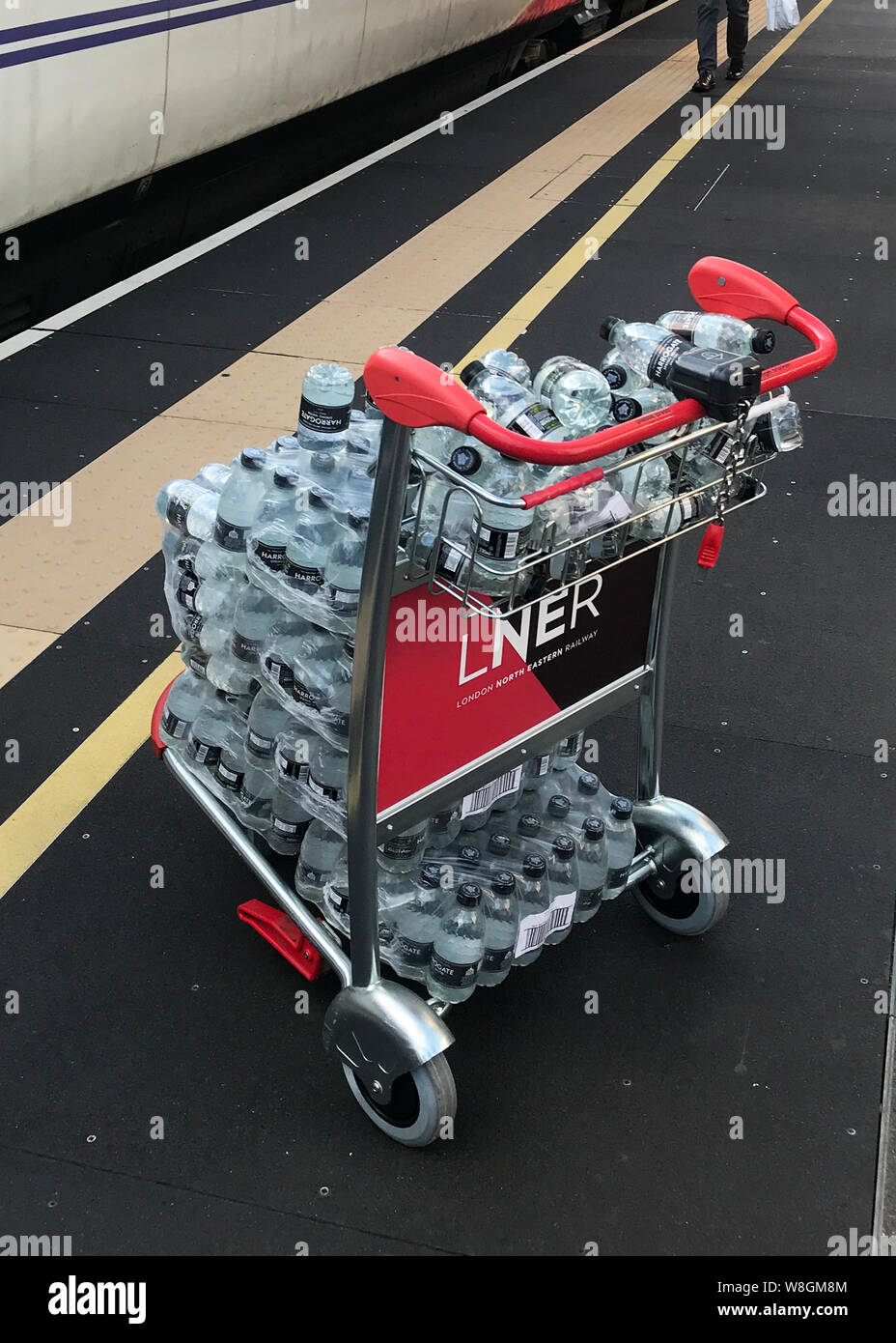 A trolley of bottled water next to an LNER train, as passengers wait ...