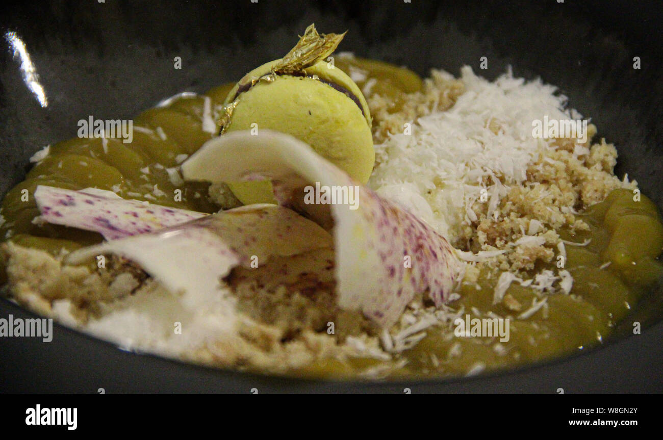 A closeup of a black plate with a mango pave, with coconut, a macaron ...